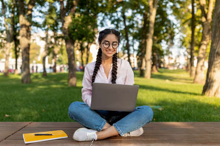 E-learning concept. Indian female student with laptop sitting on bench ...