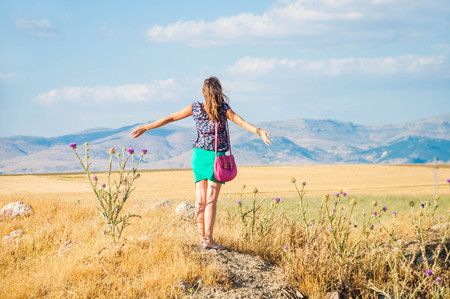 Young happy woman from back in the field is open to the whole world ...