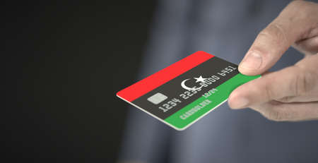 Man gives bank card with printed flag of Libya. Fictional numbers ...