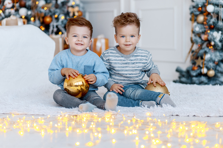 Twin brothers in front of the christmas tree with candles and gifts ...