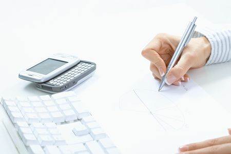 Female hand holding pen, writing on paper, beside desktop computer keyboard and mobile phone.の写真 ...