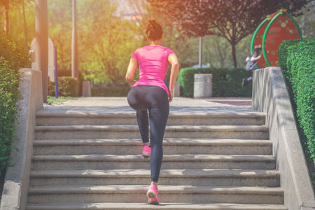 Muscular sportswoman running up on stairs. Morning workout. Urban scene ...