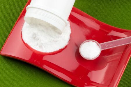 Creatine monohydrate powder in measure spoon on a red saucer. Sport ...