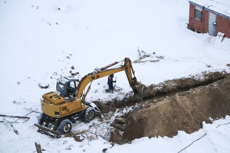 Excavator digs frozen land covered with snowdrifts. preparation of the ...