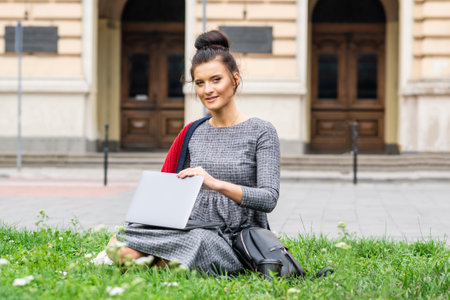 Portrait of a beautiful young smiling student studying with a laptop on ...