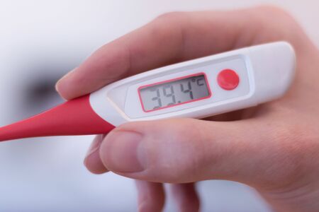 Man holds a red fever thermometer with 39 degrees Celsius in his hand ...