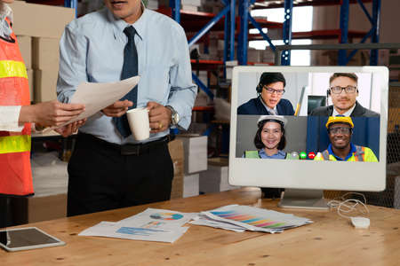 Warehouse staff talking on video call at computer screen in storage ...