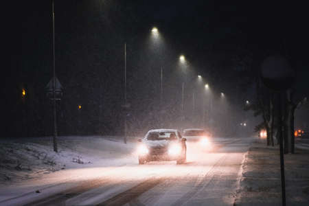 Cars in a snowstorm at night on the road in winter. Traffic in winter ...