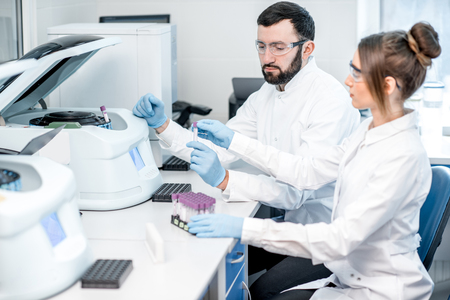 Laboratory assistants making analysis with test tubes and analyzer ...