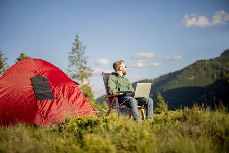 Man works on laptop while traveling with tent in the mountains ...