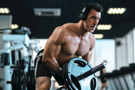 Closeup portrait of a muscular man workout in headphones with barbell ...