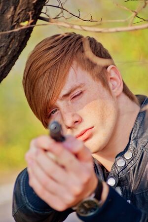 attractive, aggressive red-haired guy with a gun in nature. close-up ...