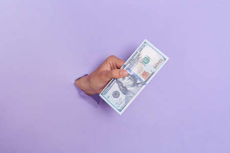 One hundred dollar banknotes in human's hand breaking through purple ...