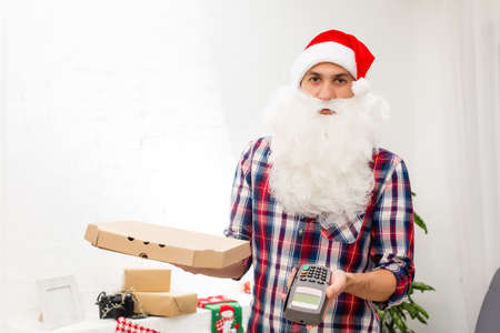 Smiling Santa Claus stands box of pizza in her hands and pos terminal ...