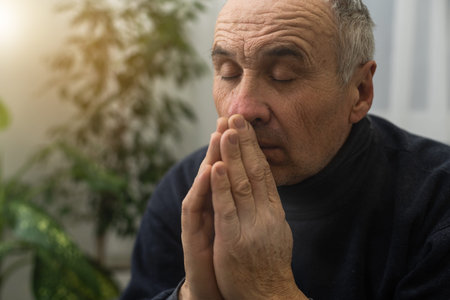Worried religious senior man praying to god with his hands raised and ...