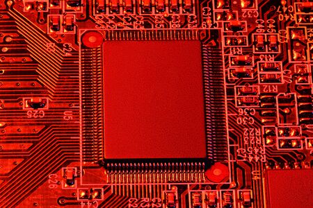 printed circuit board and microchip, or cpu, in red light closeup ...