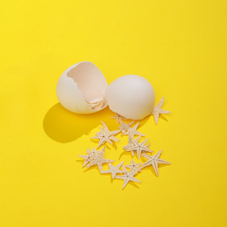 Creative layout with starfish and eggshell on bright yellow background ...