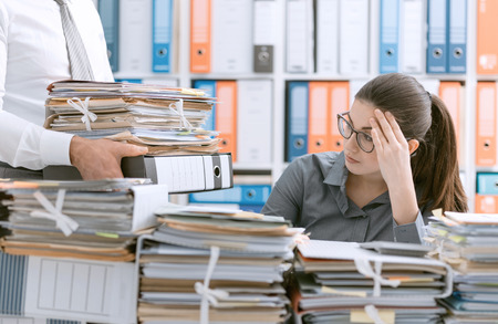 Young stressed secretary in the office overwhelmed by work and desk ...
