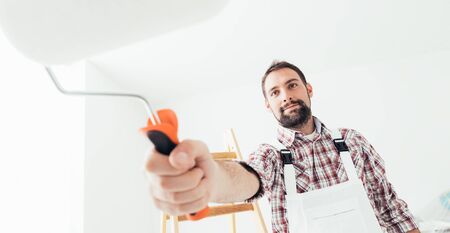 Smiling professional painter working and painting, paint roller on the ...