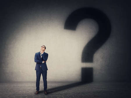 Pensive businessman casting an interrogation mark shadow on the wall ...