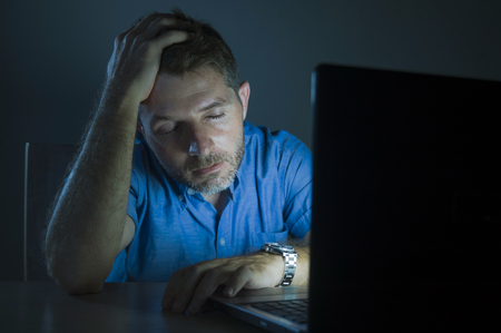 young attractive and tired unshaven man working late night on laptop ...