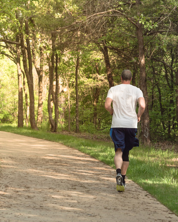 Rear view of senior Caucasian man running at nature park during sunset ...