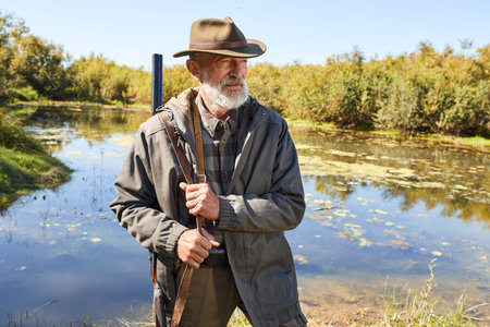 Senior caucasian man hunting on ducks, holding rifle and look away ...