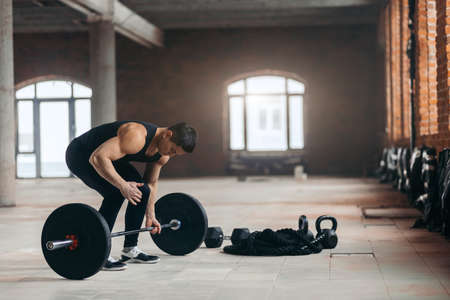 man is going to lift a barbell with one arm. full length side view ...