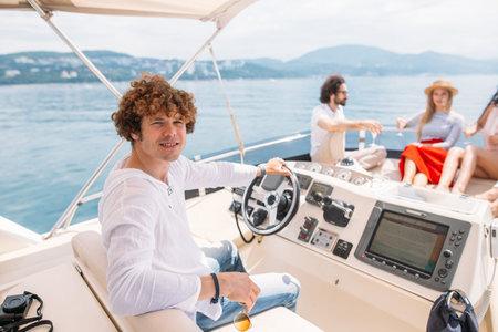 Young handsome curly captain navigatong sailing boat and looking at ...