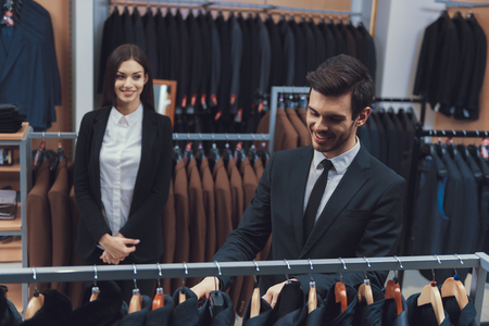 Confident young man looks at jackets for sale in showroom of men ...