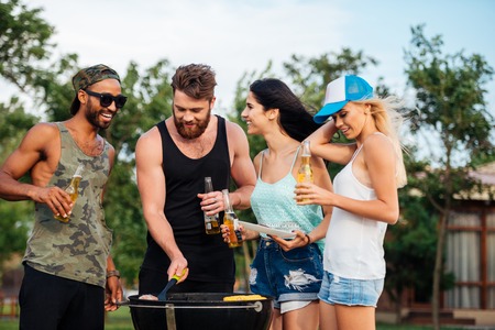 Group of happy young people standing and frying meet on barbeque grill ...