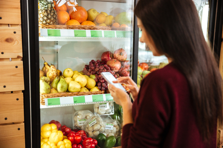 Back view of woman standing and using cell phone in grocery shop ...