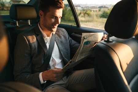 Charming businessman reading newspaper while sitting at the back of a ...