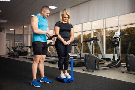 A person stands on the scales, coach records the results of weight loss ...