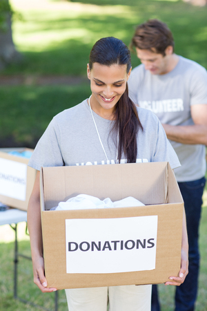 Happy volunteer brunette holding donation box on a sunny day - Stock ...