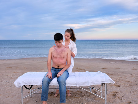 A young man with bare torso sitting on a massage table receiving a ...