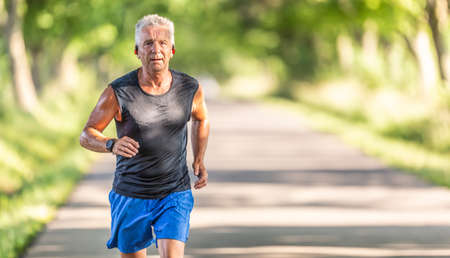 Fit old man in shorts and shirt without sleeves runs outdoors in the ...