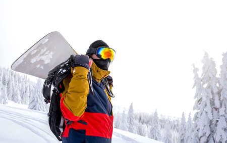 A snowboarder in protective glasses holding his snowboard on his back ...