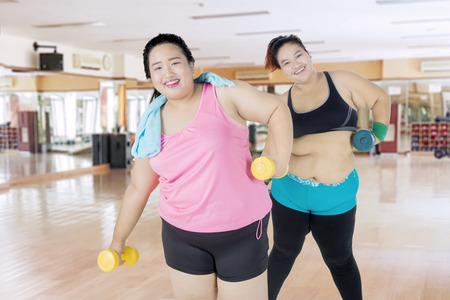 Two obese people smiling at the camera while exercising with dumbbells ...