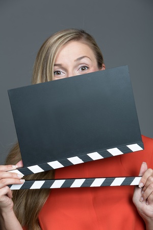 Woman with a blank clapper slate hiding the lower portion of her face ...