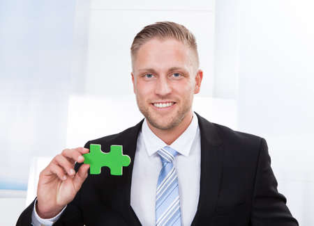 Successful businessman holding a green puzzle piece as he indicates he ...