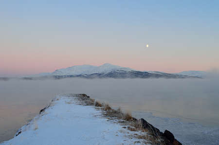 beautiful stone pier going out in a icy fjord covered in thick ice fog ...