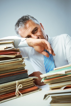 Stressed businessman, with a too much paperwork and files piled up on ...