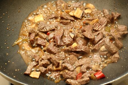 beef meat stewing with red peppers in black frying pan - Stock Image ...