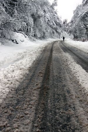 A man walking down a winter snow covered road through rural forest ...